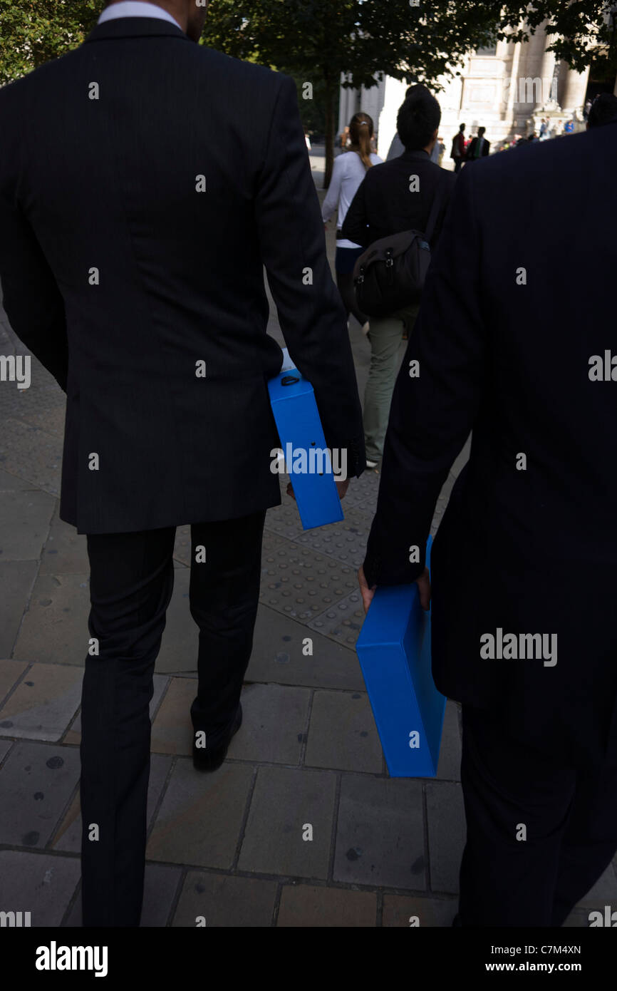 Two businessmen in dark formal suits carry identical blue boxes along a ...