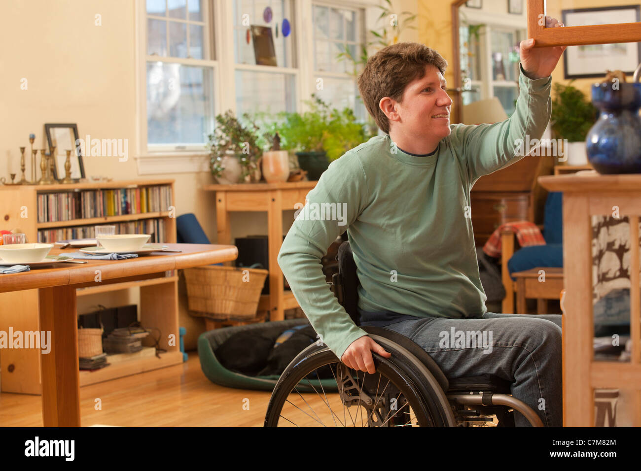Woman With Multiple Sclerosis In A Wheelchair Getting Table Settings From Accessible Cupboard
