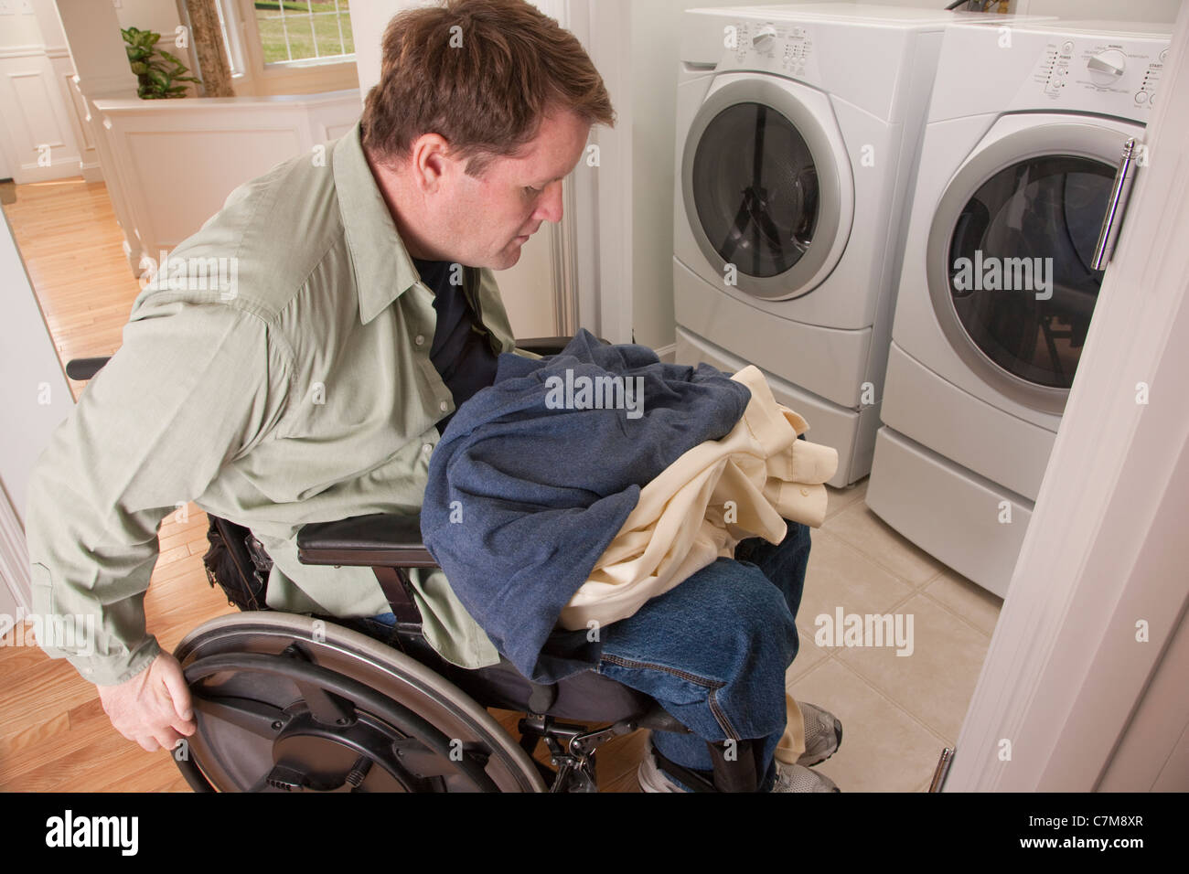 Man with spinal cord injury in a wheelchair doing his laundry at home ...