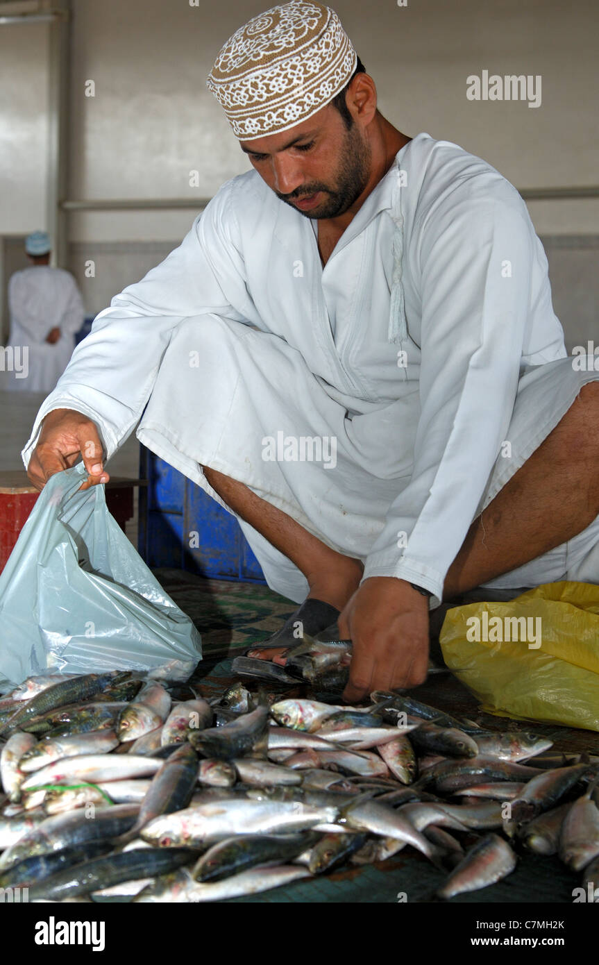 Arab man in traditional garment buying fish on a fish market, Sur ...