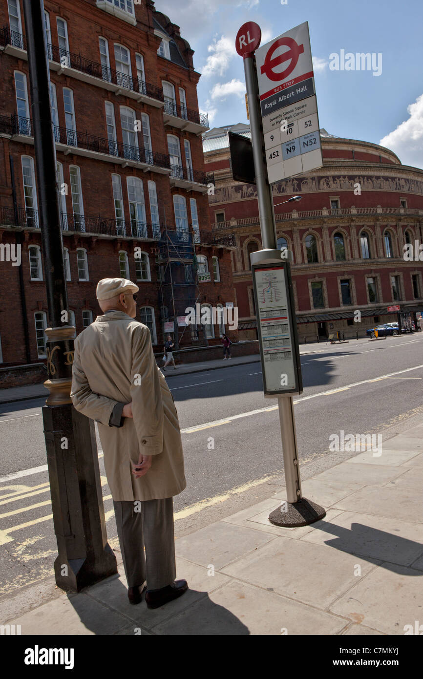Senior man standing at bus stop next to Royal Albert Hall, London ...