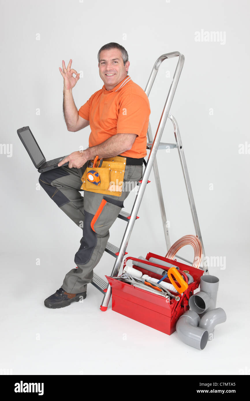 Labourer sat on ladder holding laptop computer Stock Photo - Alamy