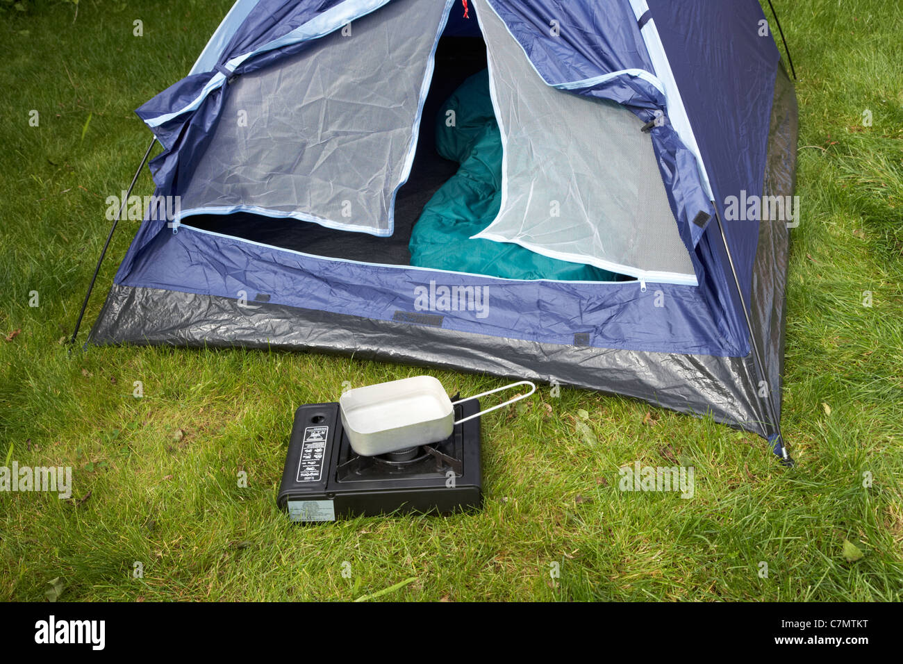 boiling water in a mess tin on a gas camping stove in front of a tent ...
