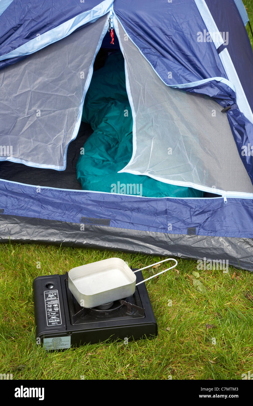 boiling water in a mess tin on a gas camping stove in front of a tent ...