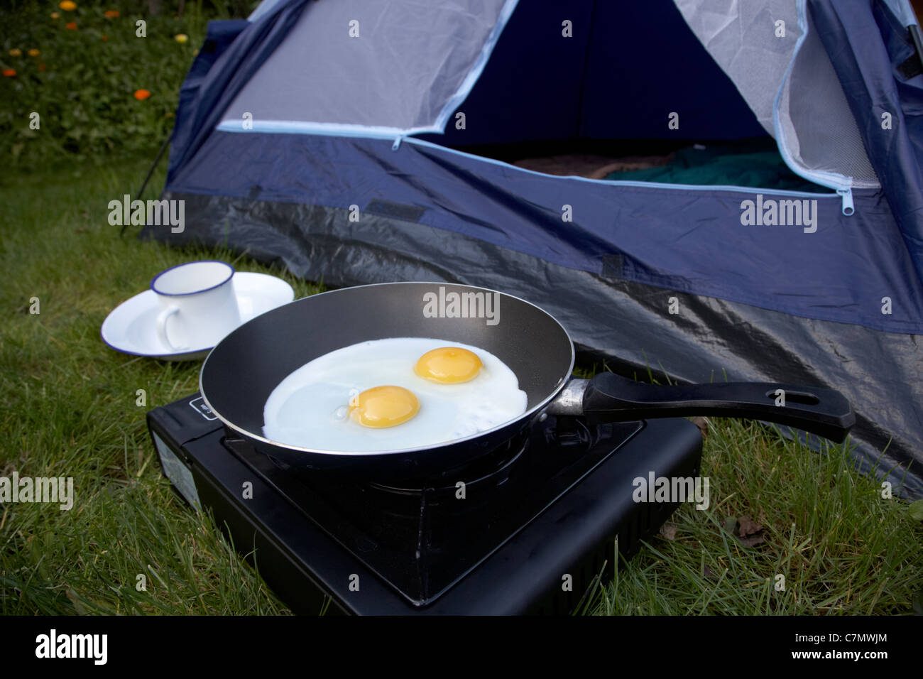 cooking two fried eggs on a small portable gas camping stove in front ...