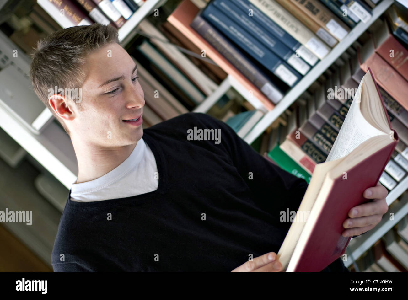 A young college aged man reading a book at the library Stock Photo - Alamy