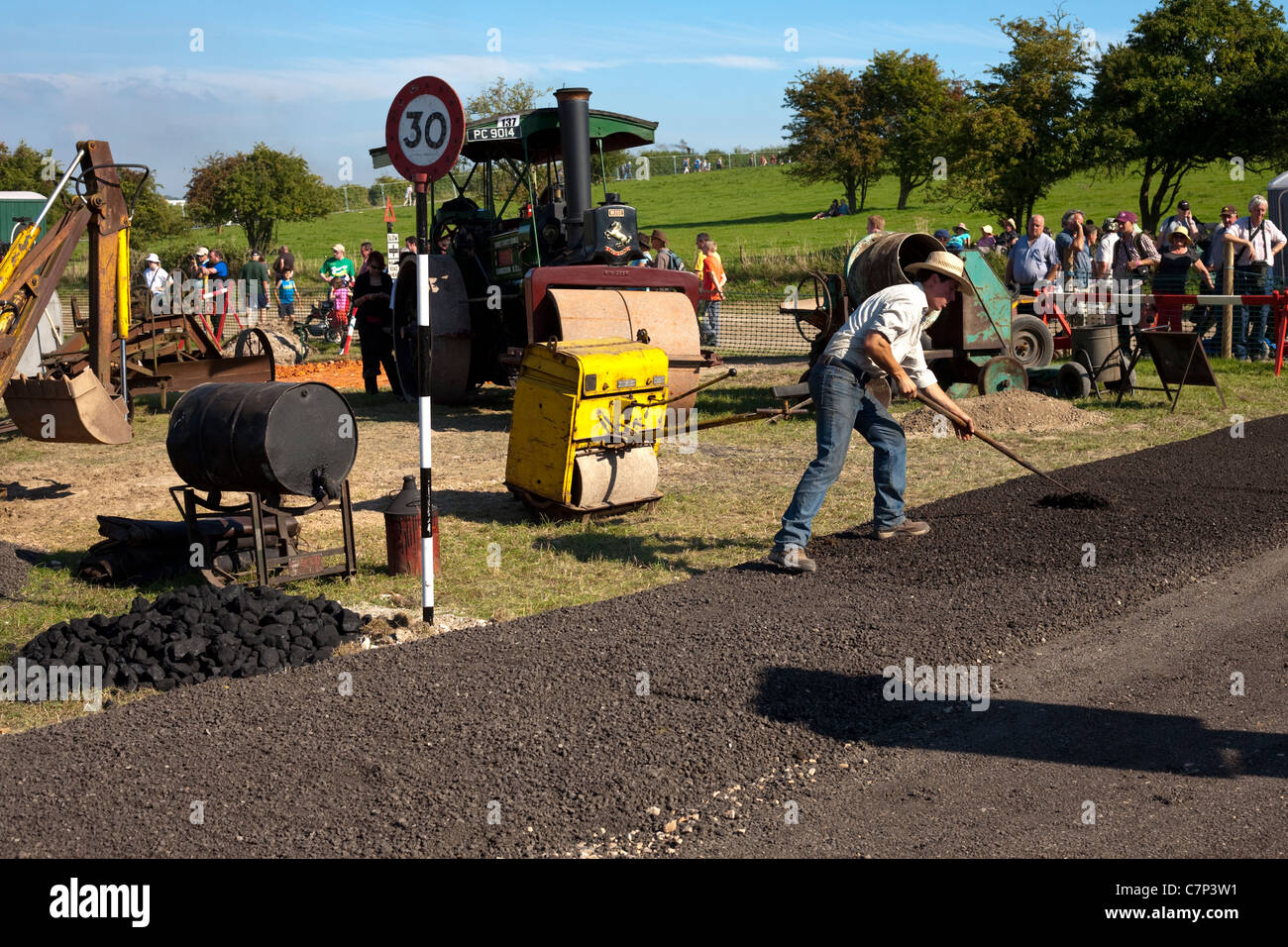 man demonstrating tarmac laying with steam roller in background and ...