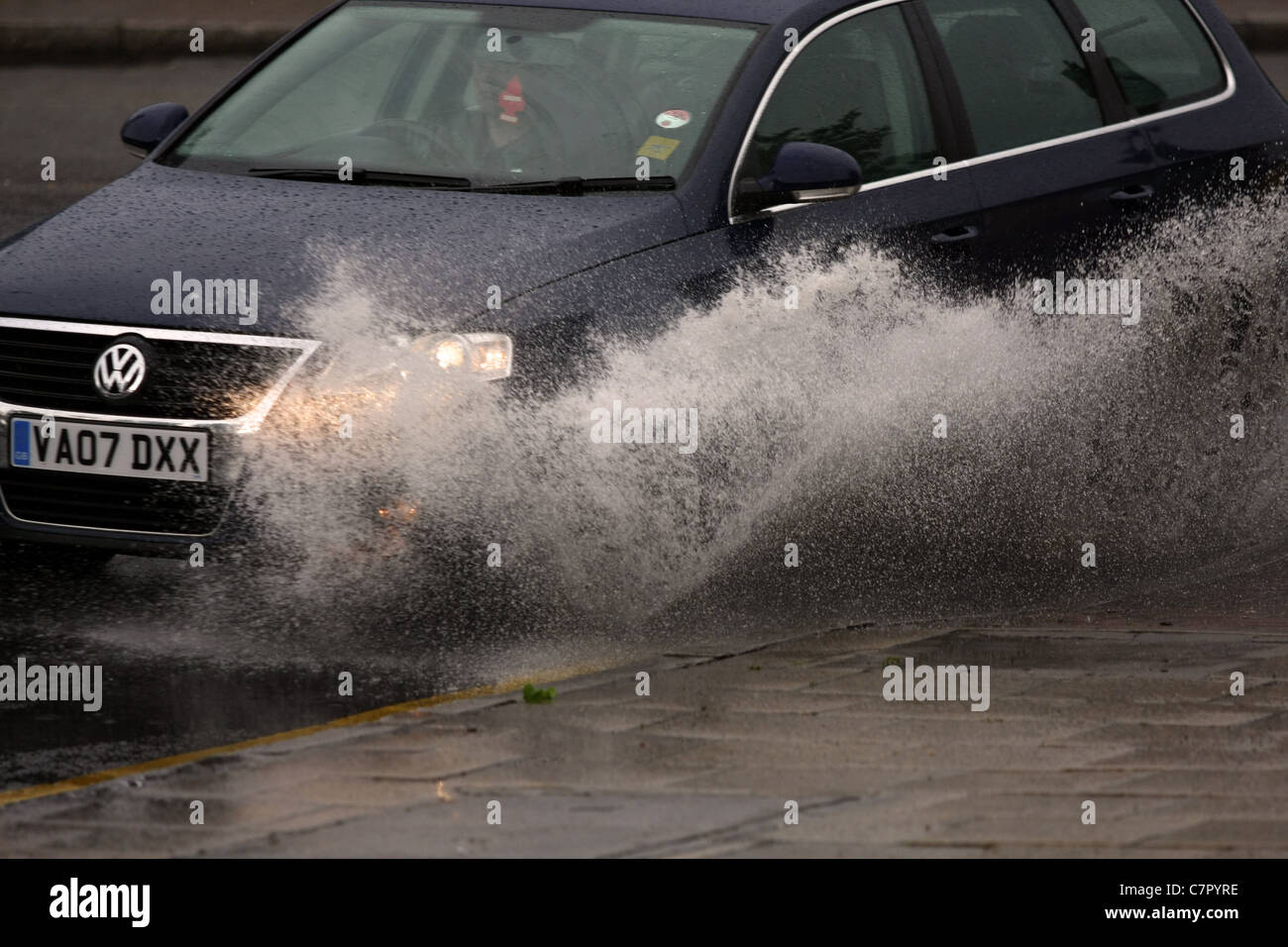 a car splashing through a puddle on the side of a road in London Stock ...