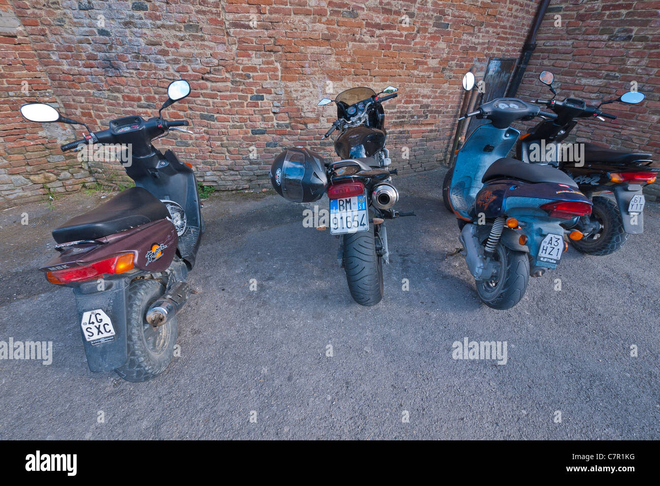 Four motorcycles parked against brick wall viewed from the rear in ...