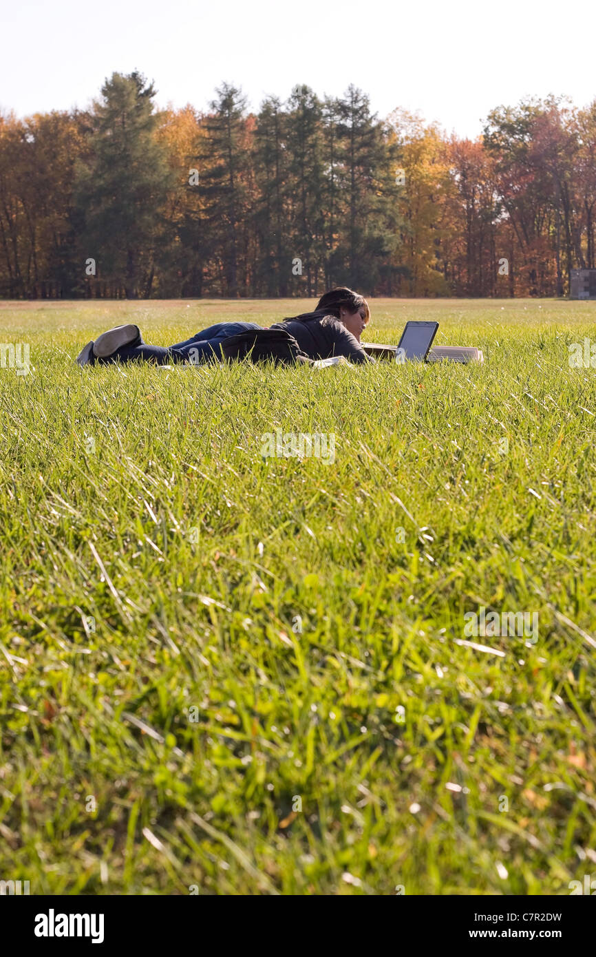 A young student using her laptop computer while laying in a green ...