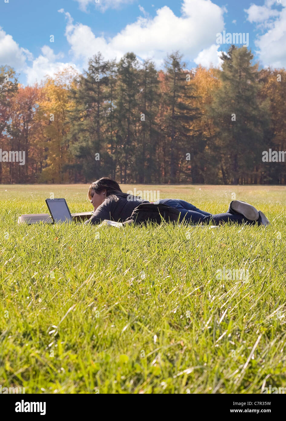 A young student using her laptop computer while laying in a green ...