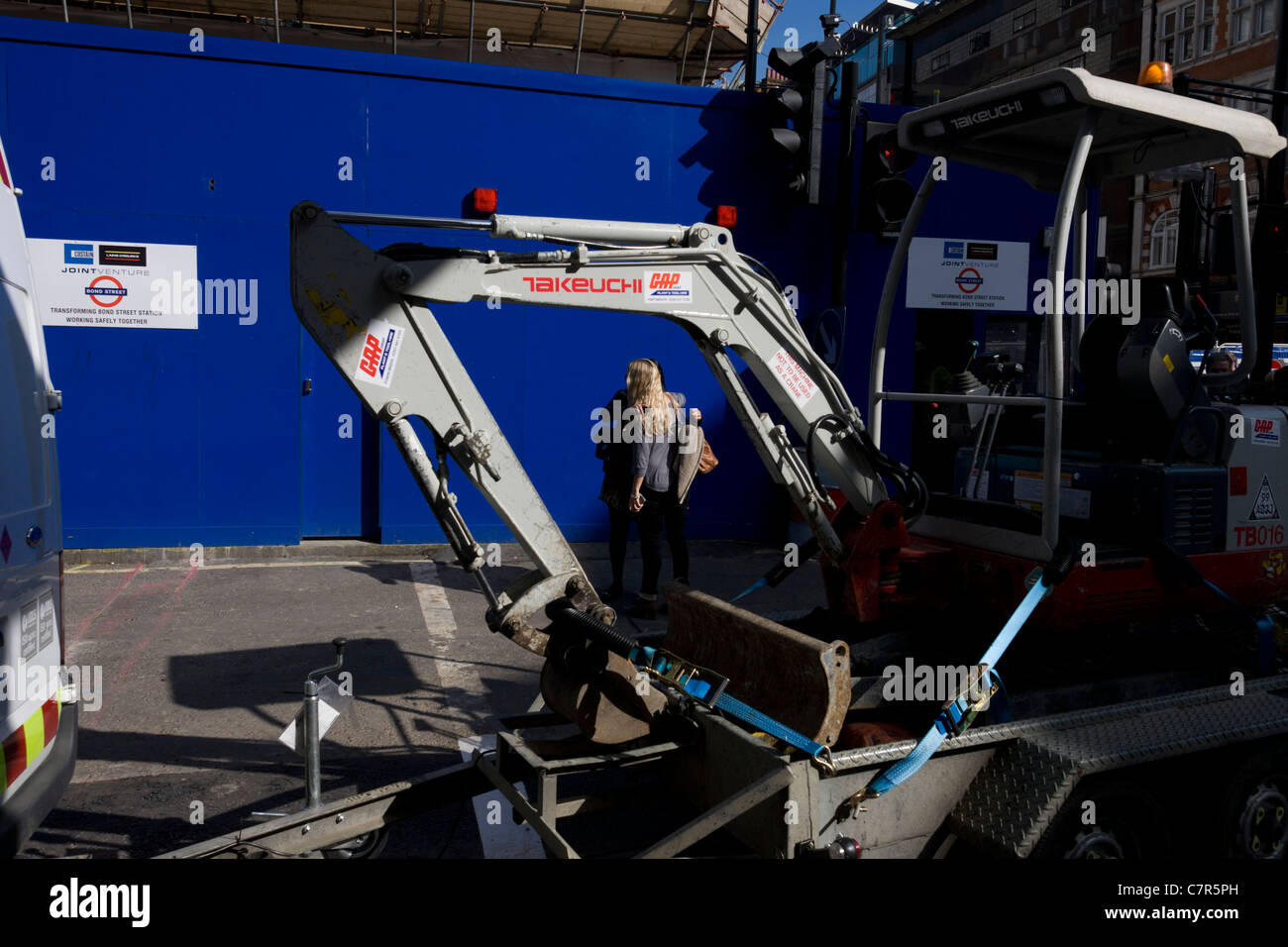 Seen through the folded arm of a small excavator, two friends hug ...