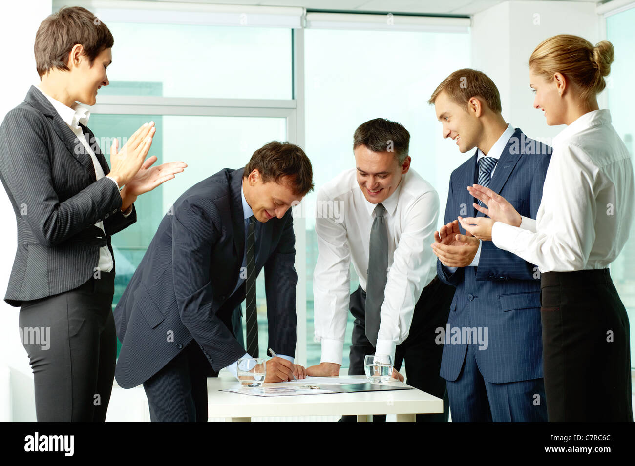 Image of co-workers congratulating their colleague while he signing ...