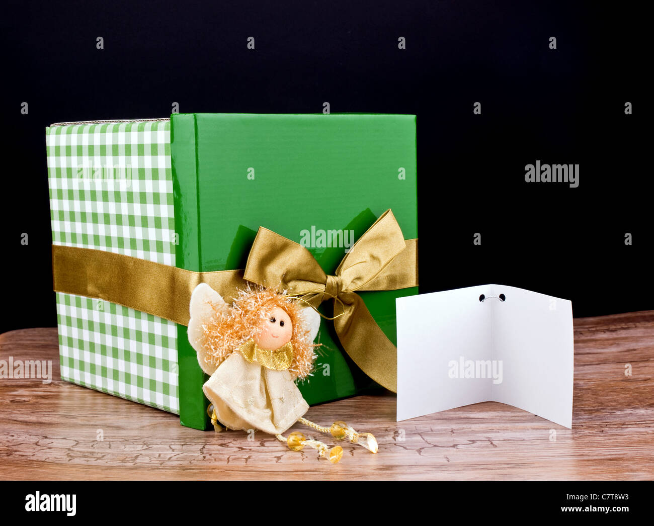 Big green gift box with golden ribbon and little angel on wooden table ...