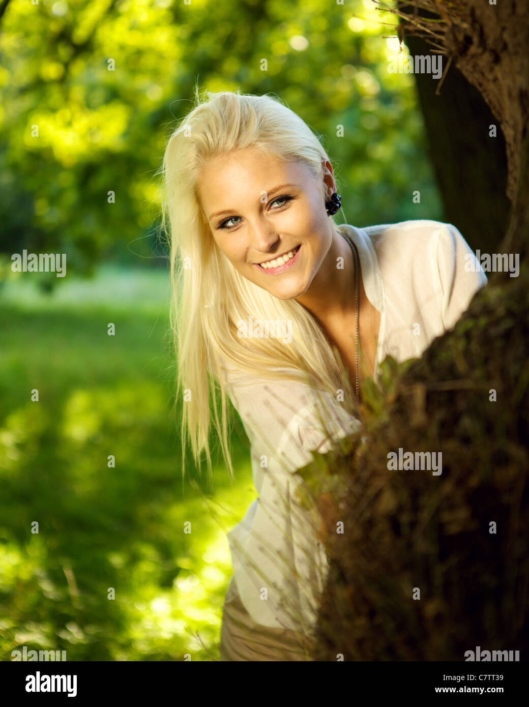 Portrait of a natural and cute female hiding behind a tree in a park ...