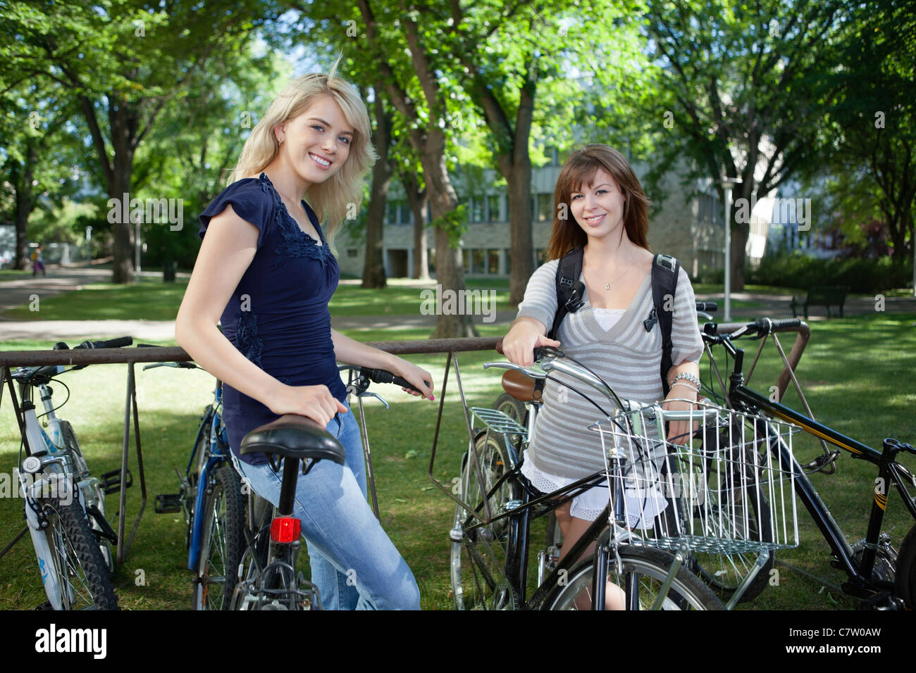 Young female students standing with bicycle at college campus lawn ...