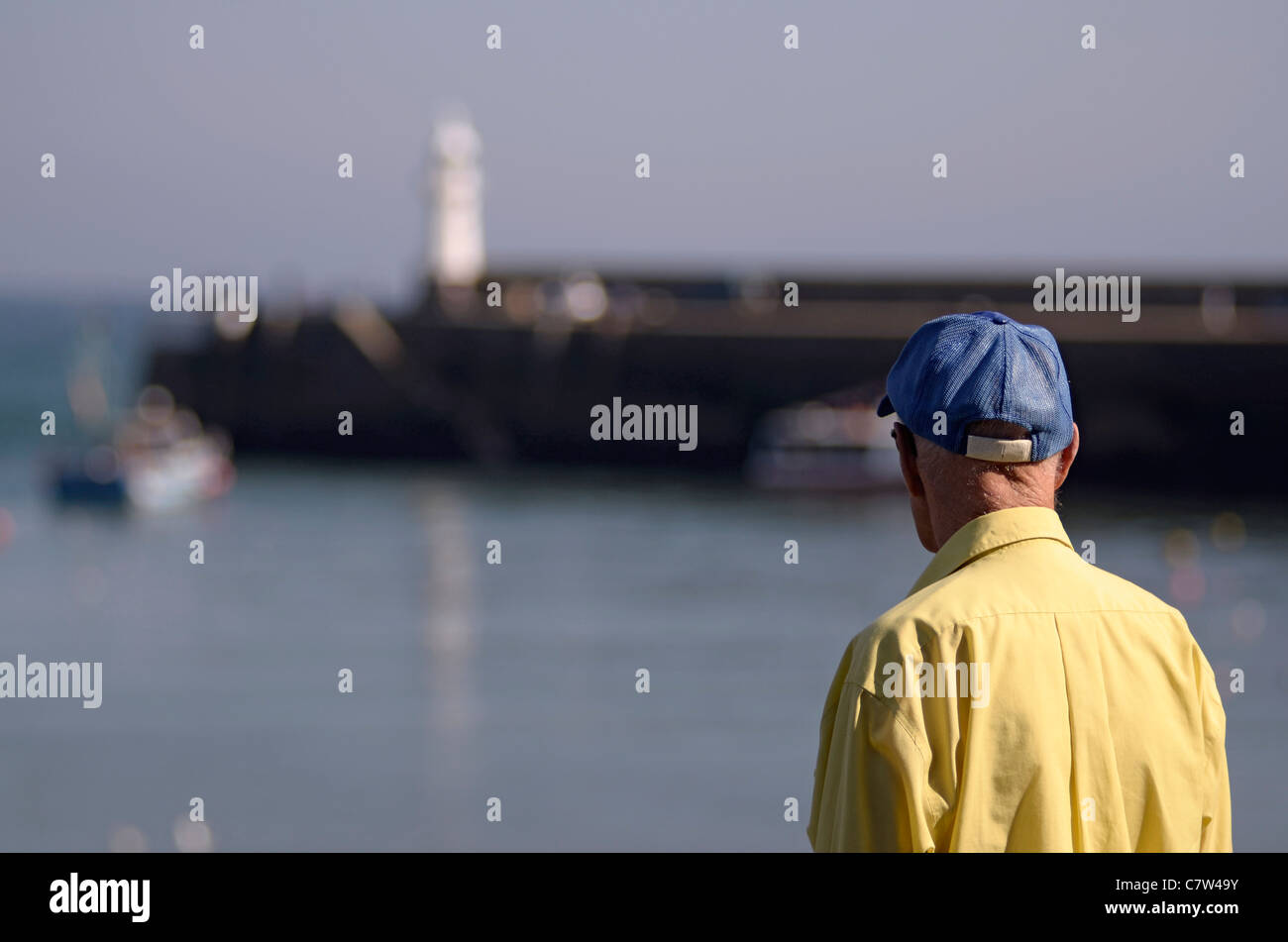 Retired man in baseball cap looking at Mevagissey harbour Cornwall UK ...