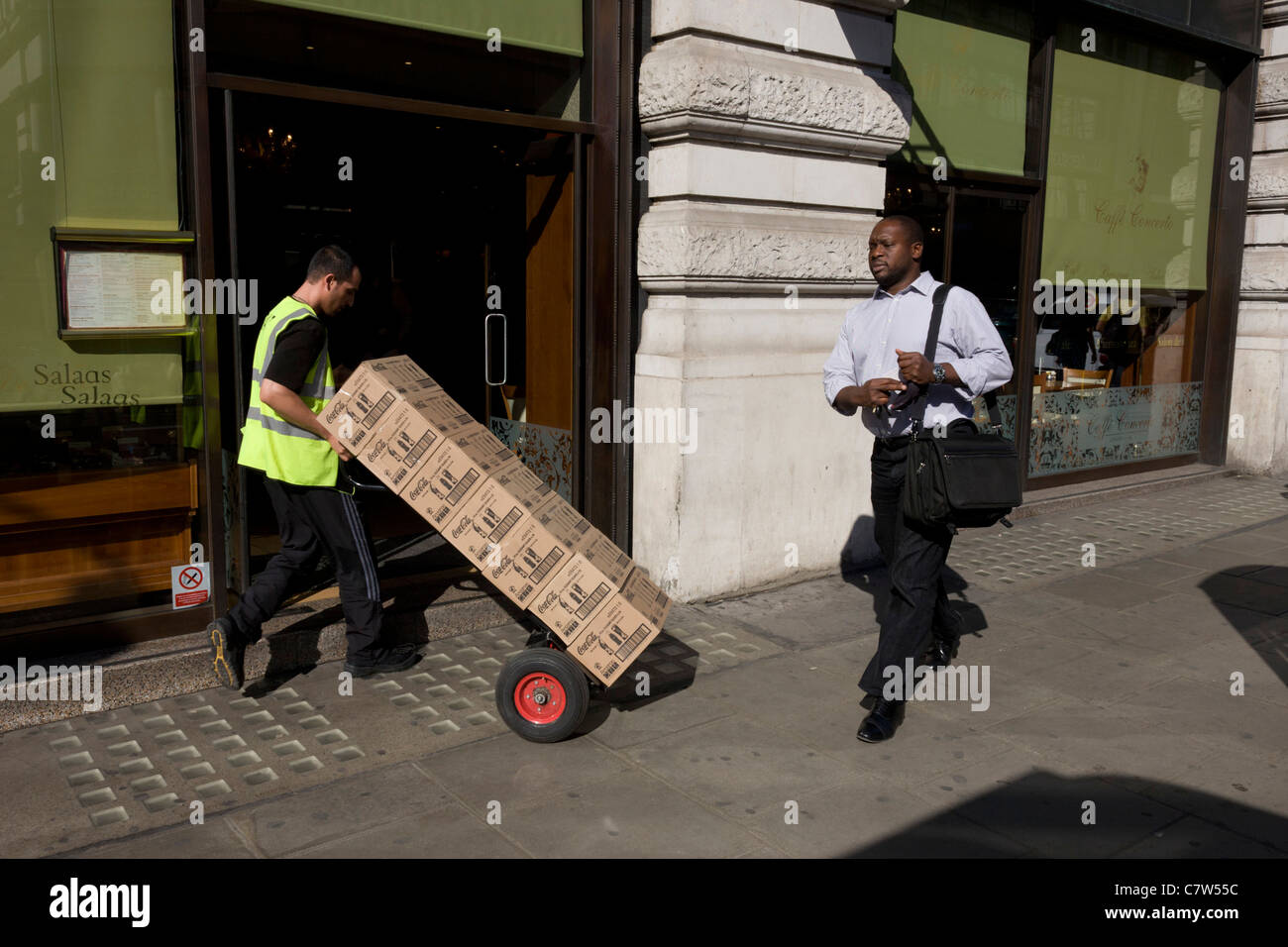 An educated businessman walks past a manlual labour delivery man ...