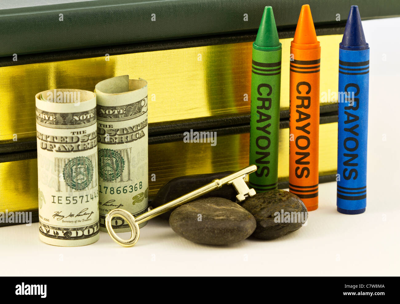 Gold key is placed on rocks that are next to money and crayons with ...
