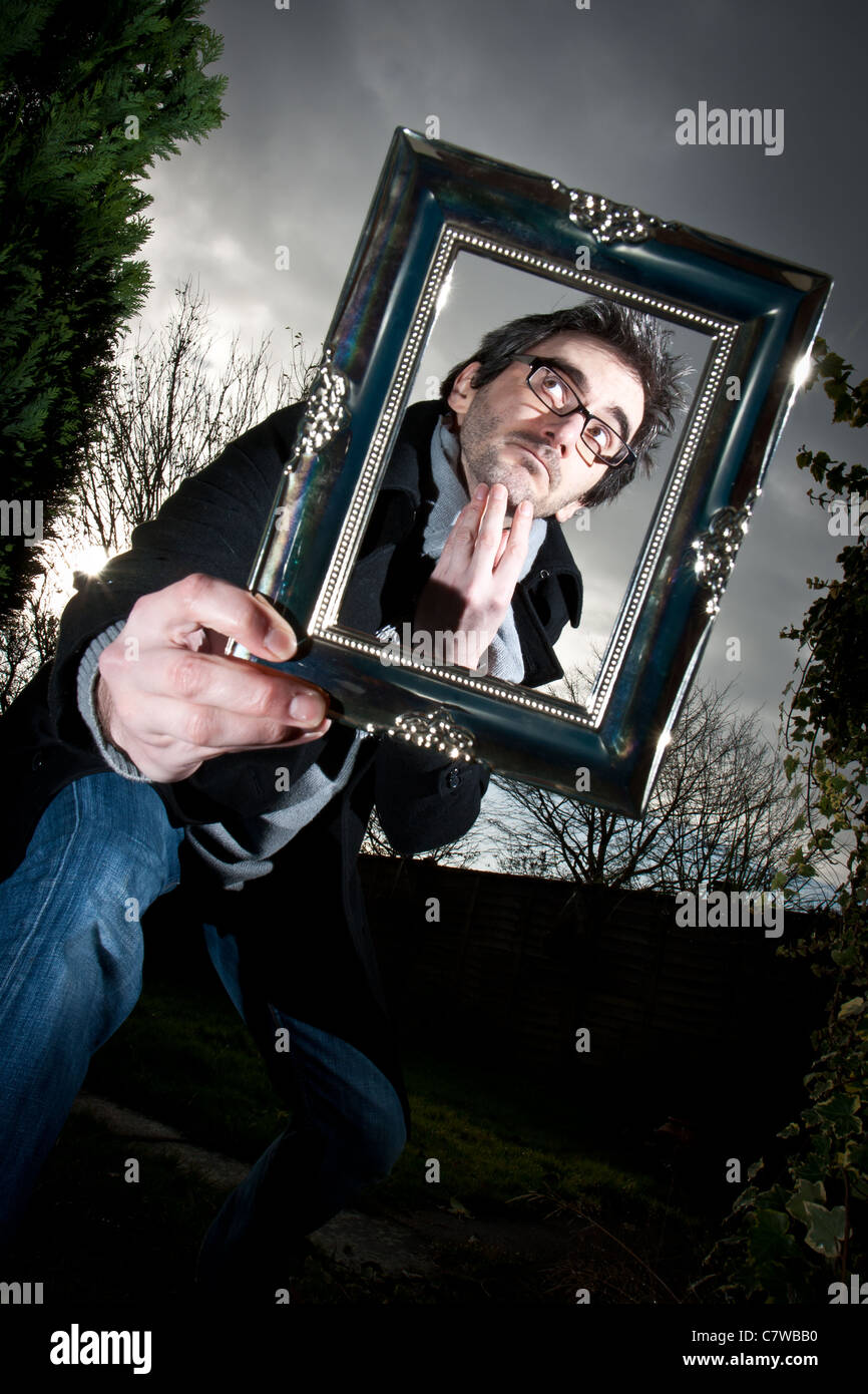 Man holding empty silver picture frame in front of his face looking ...