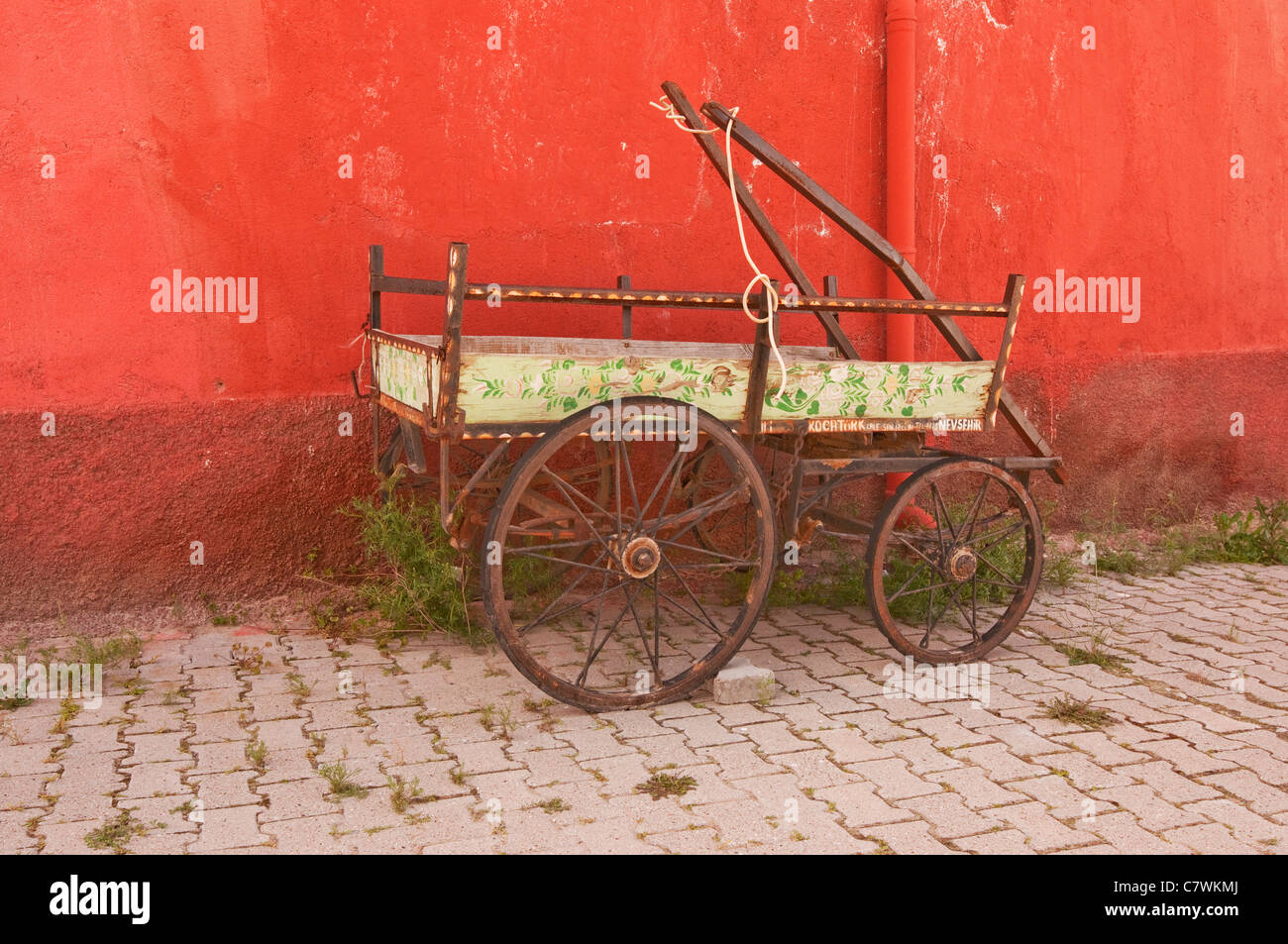 Old wooden cart with painting on side, against a red wall, Çavusin ...
