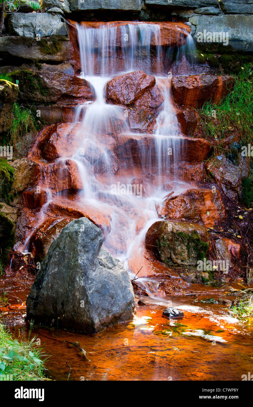 The cascading waters of a beautiful waterfall flow down over red algae ...