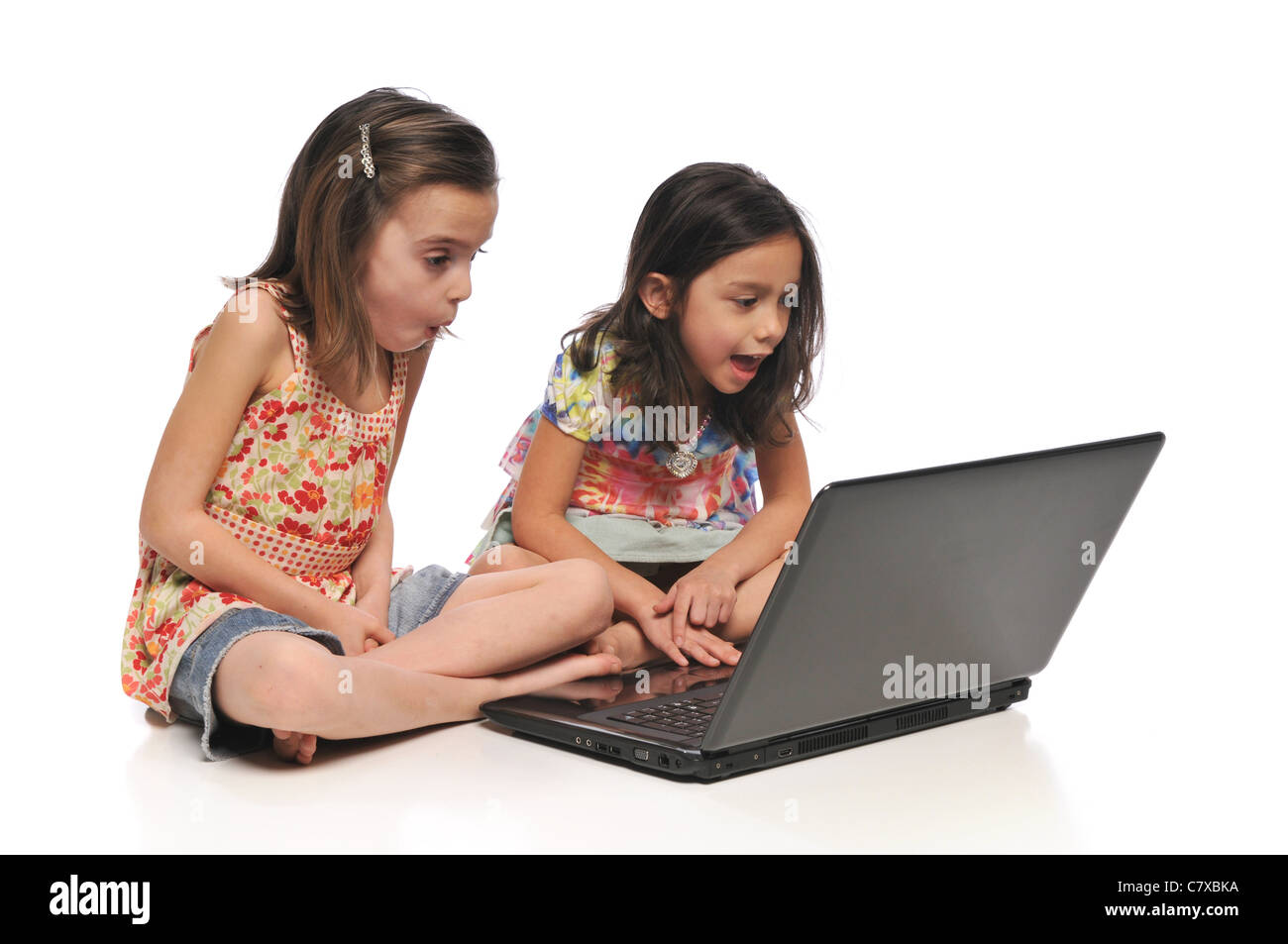 Two little girls with a laptop computer isolated on a white background ...