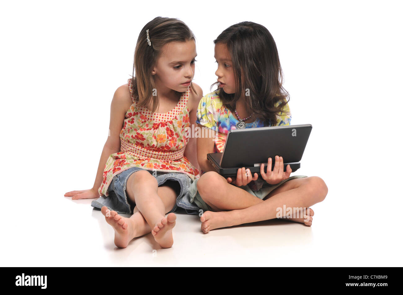 Two little girls with a laptop computer isolated on a white background ...