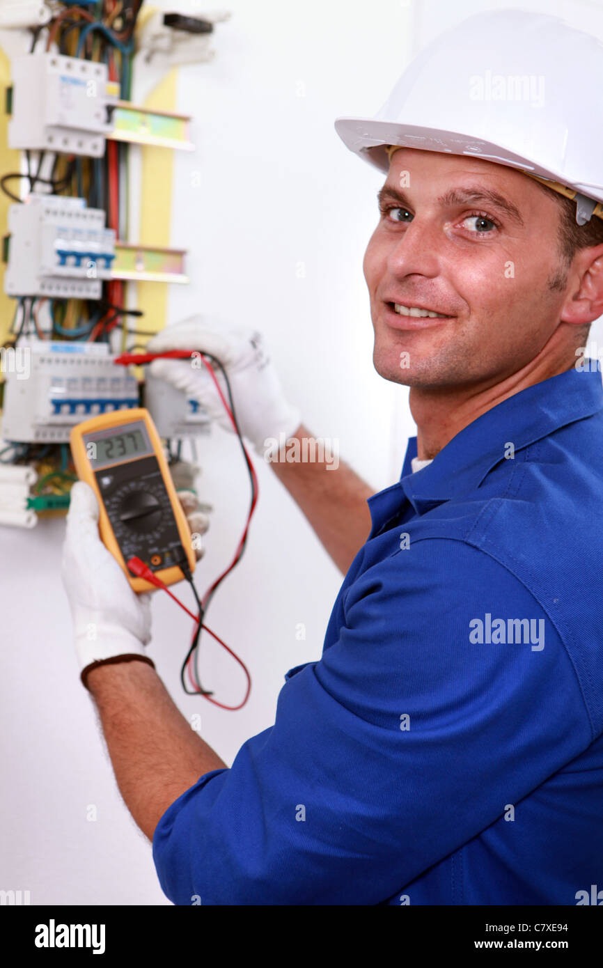 Smiling electrician using multimeter on electric meter Stock Photo - Alamy