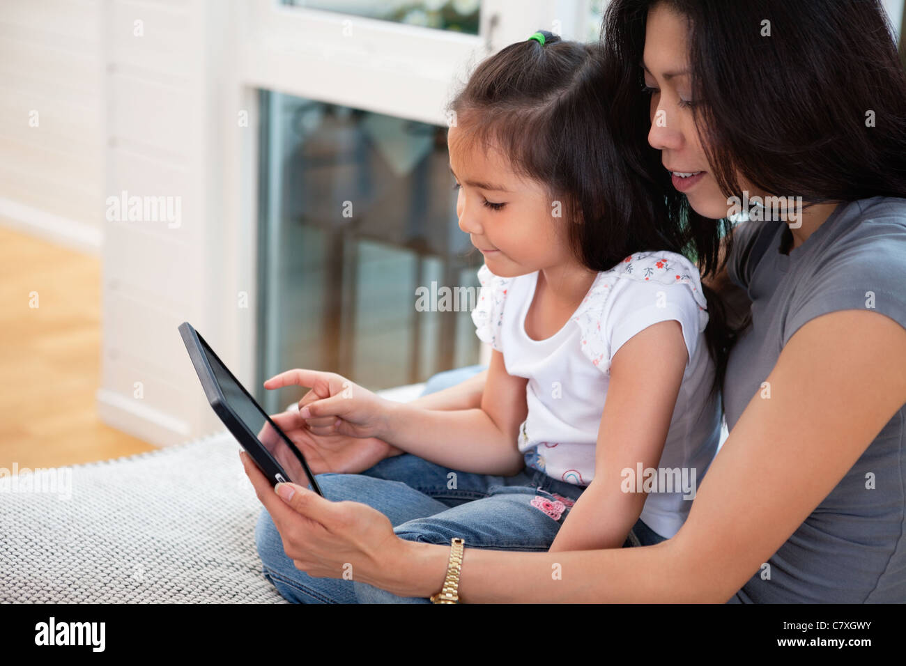 Mother and daughter reading electronic book at home Stock Photo - Alamy