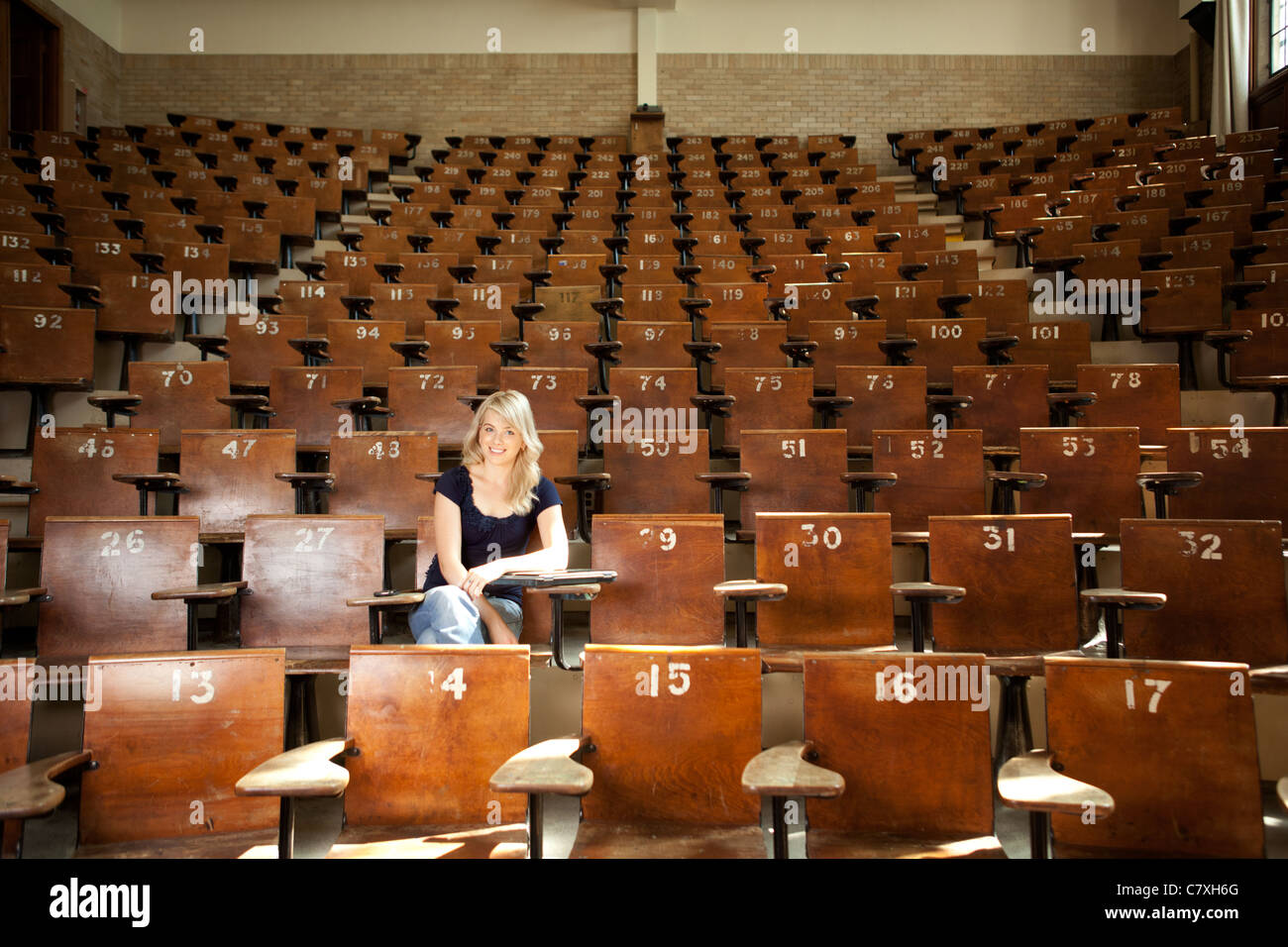 Happy blond college student alone in large lecture hall Stock Photo - Alamy