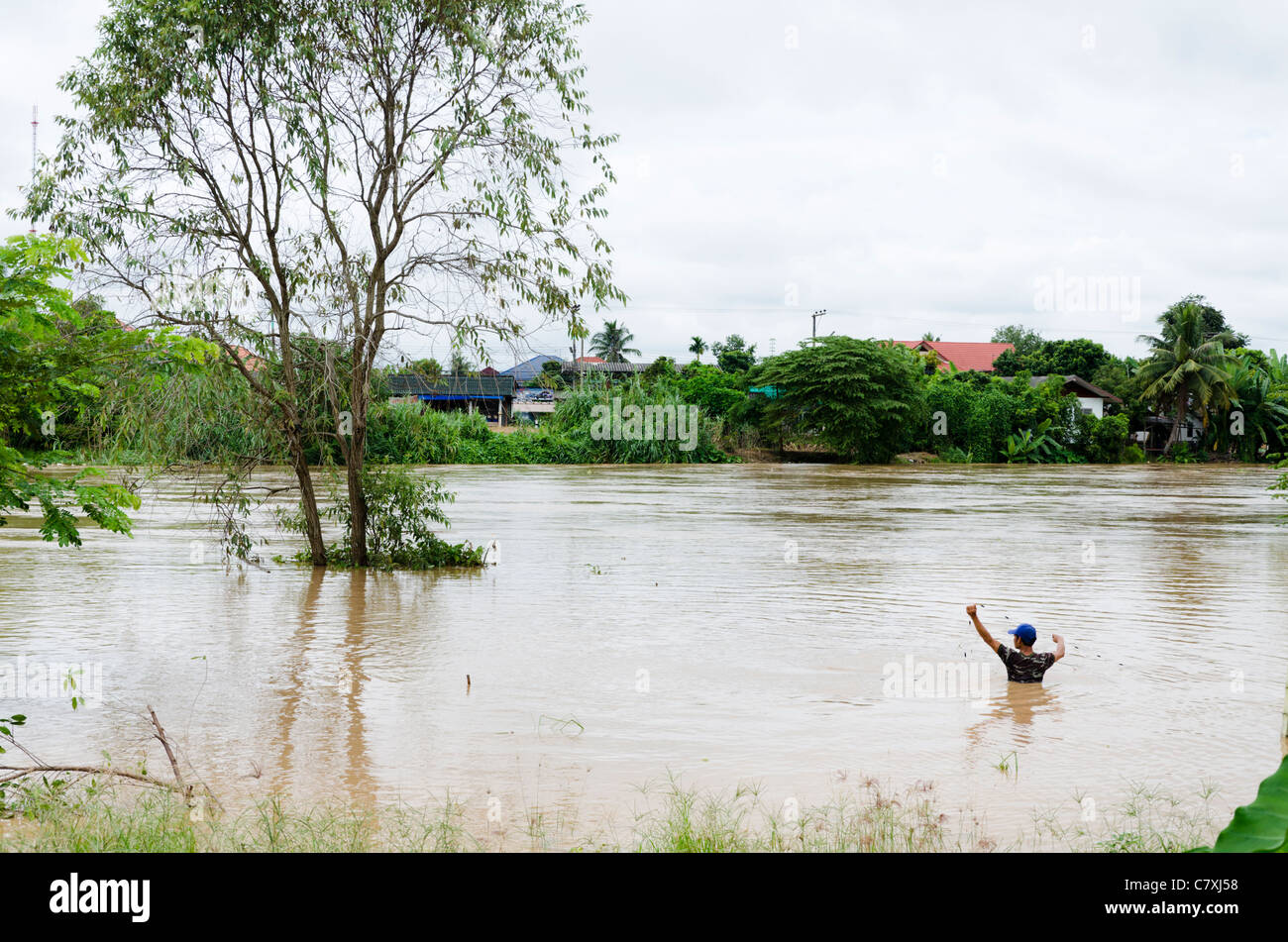 Man submerged chest deep in flooding Ping River lifts fish netting out ...