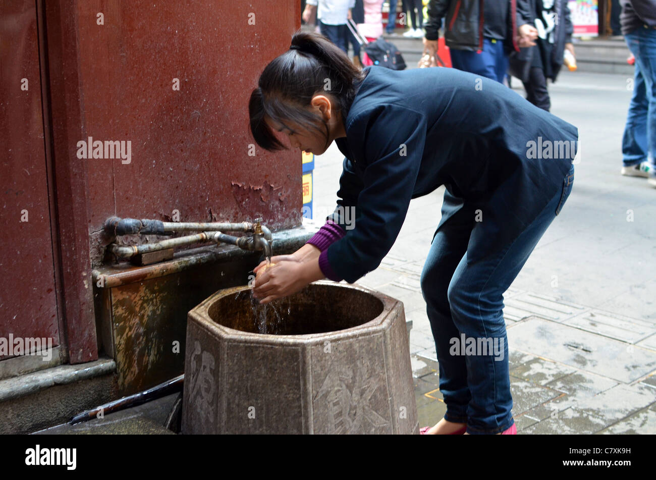 A Chinese girl washing fruit at a water tap in the street at the Yuyuan ...