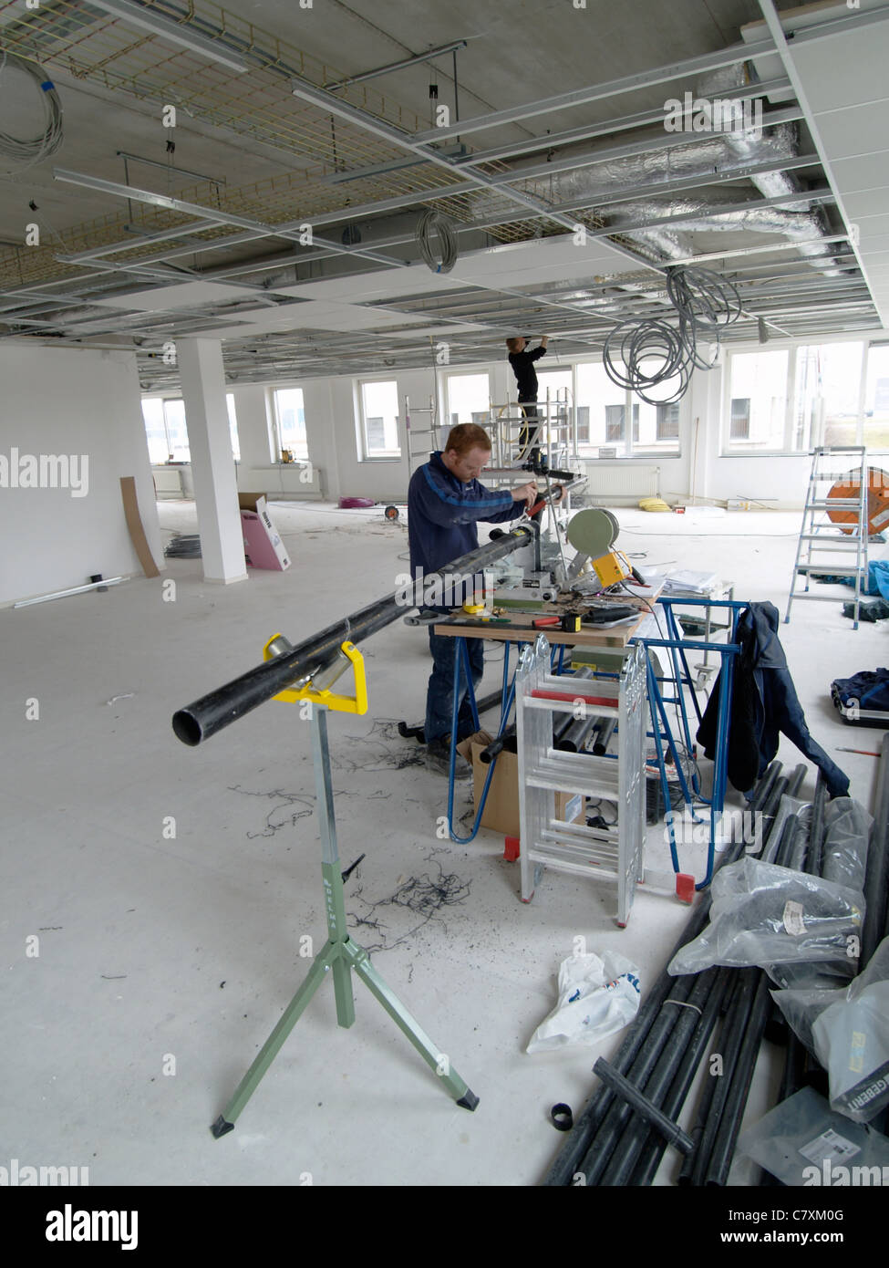 Two men installing cables and tubes in the ceiling of a brand new ...