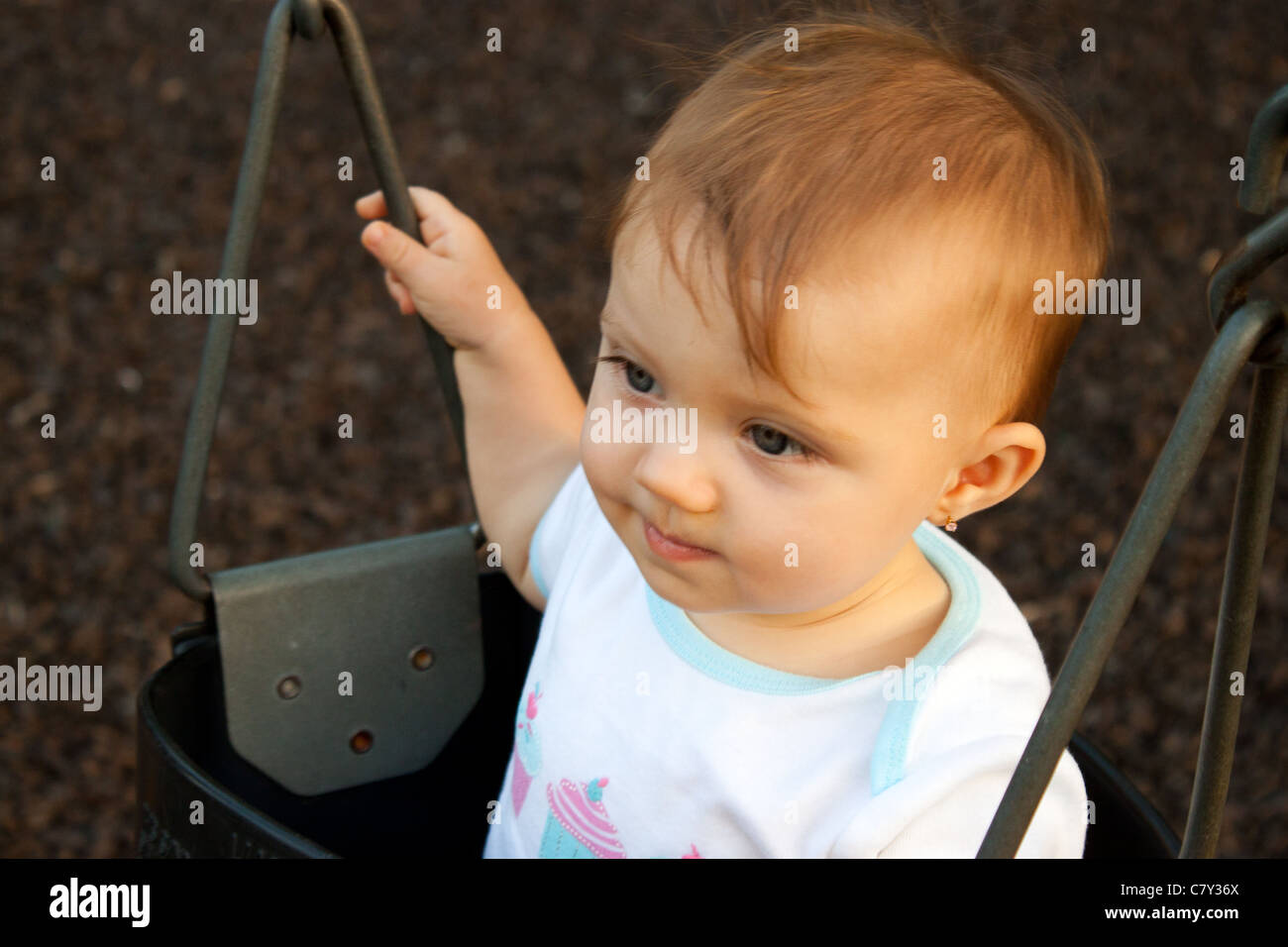 Baby girl staring forward as she swings in a park Stock Photo - Alamy