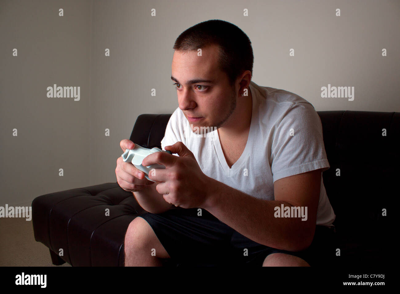 Young man playing a video game in a room lit by the television monitor ...