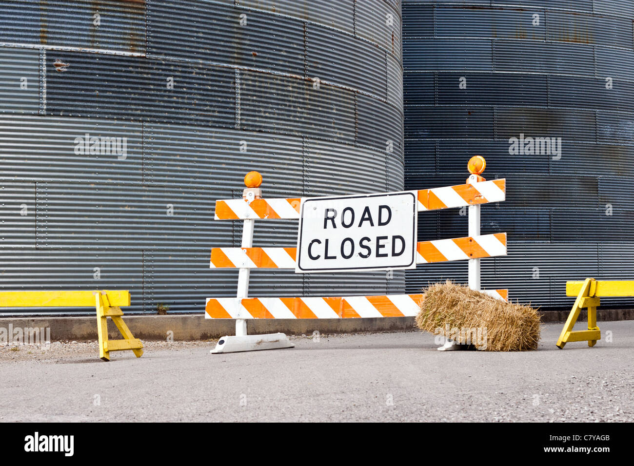 Road closed sign weighed down with hay bail in front of silos Stock ...