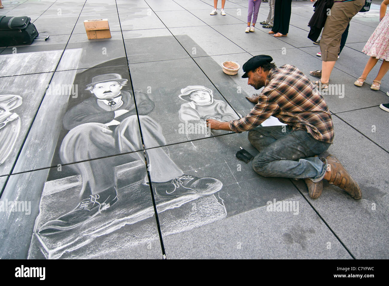 A street artist drawing Charlie Chaplin on the sidewalk with chalk ...