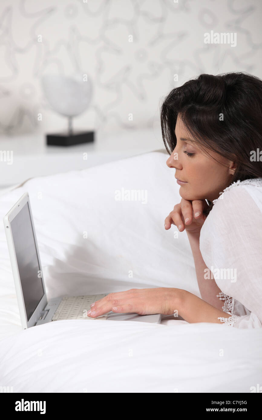 Brunette laying in bed with laptop computer Stock Photo - Alamy