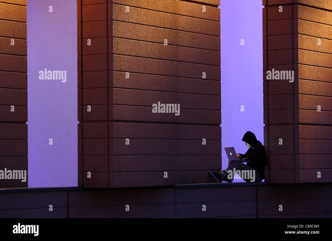 Computer user, hacker, sits conspiratorially, outside, with a laptop ...