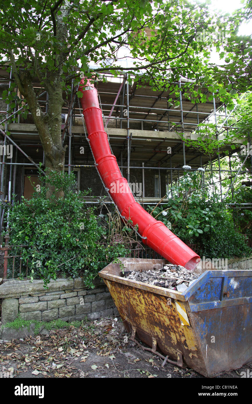 A red builders chute channeling rubble into a skip St. Just Cornwall ...