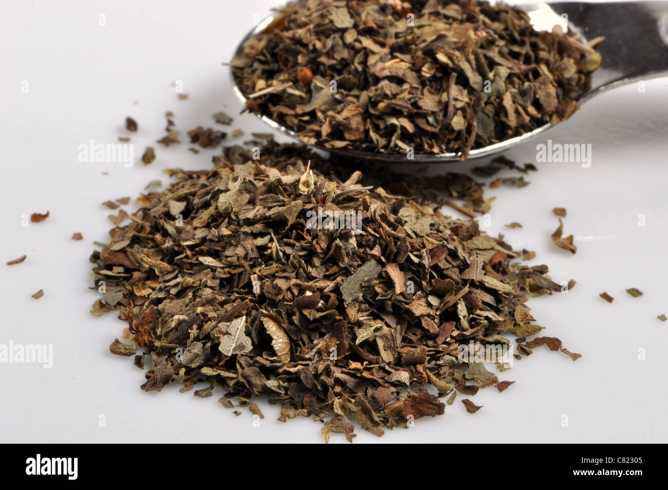 Dried basil leaves on a plain white background in a measuring spoon ...