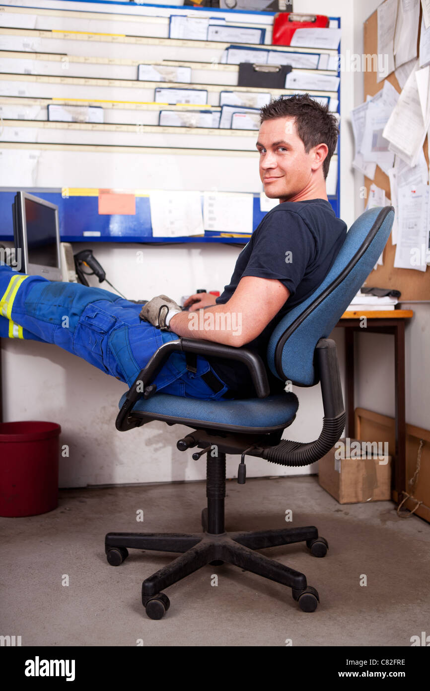 A relaxed auto mechanic leaning back in a chair in an office Stock ...