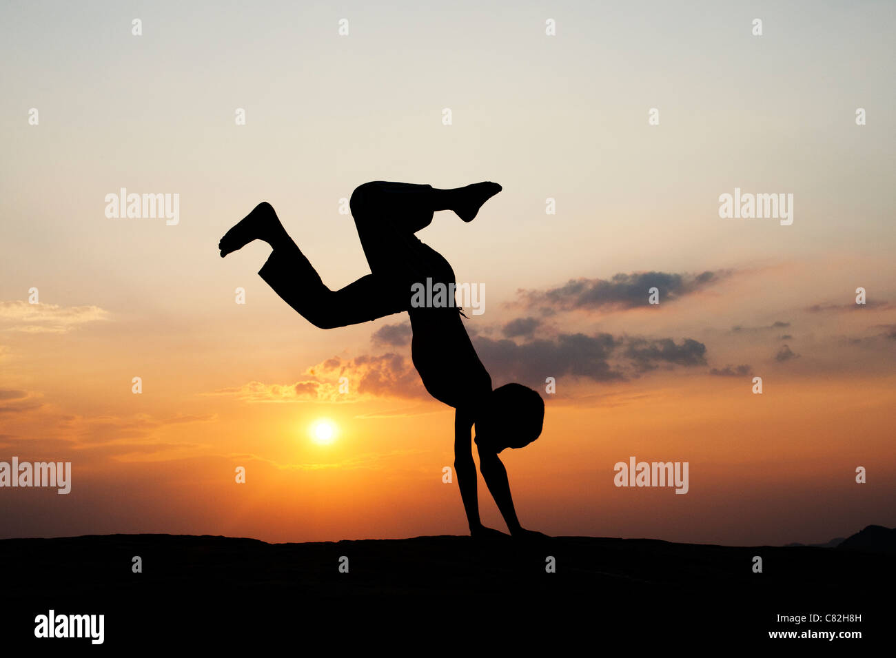 Silhouette of young Indian boy doing a handstand against a setting sun ...
