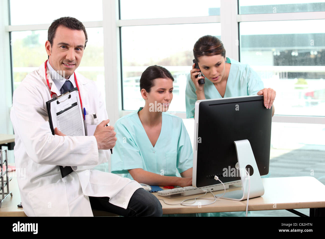 Three doctors gathered around desk Stock Photo - Alamy