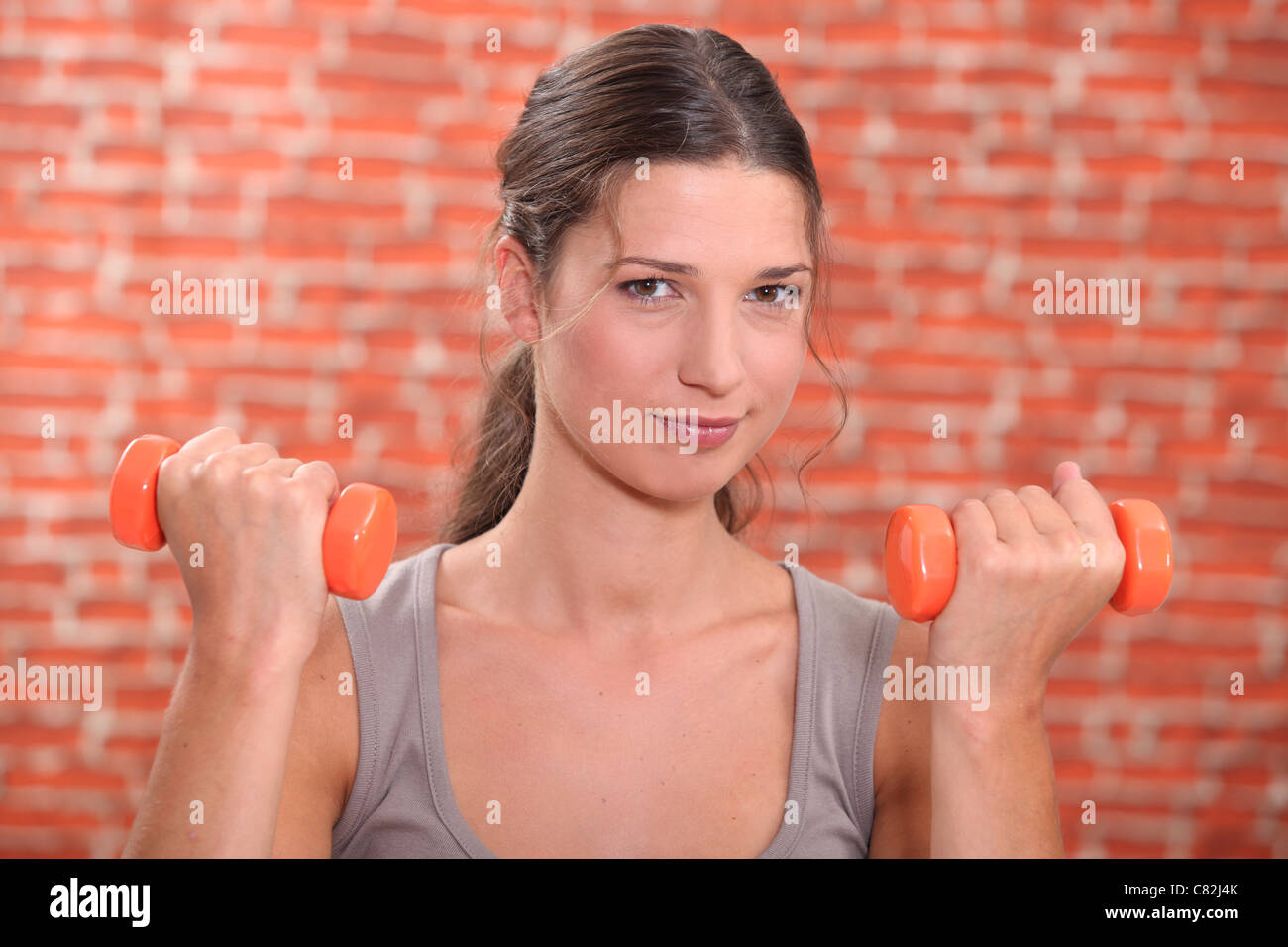 Young woman using hand weights in front of a red brick wall Stock Photo ...