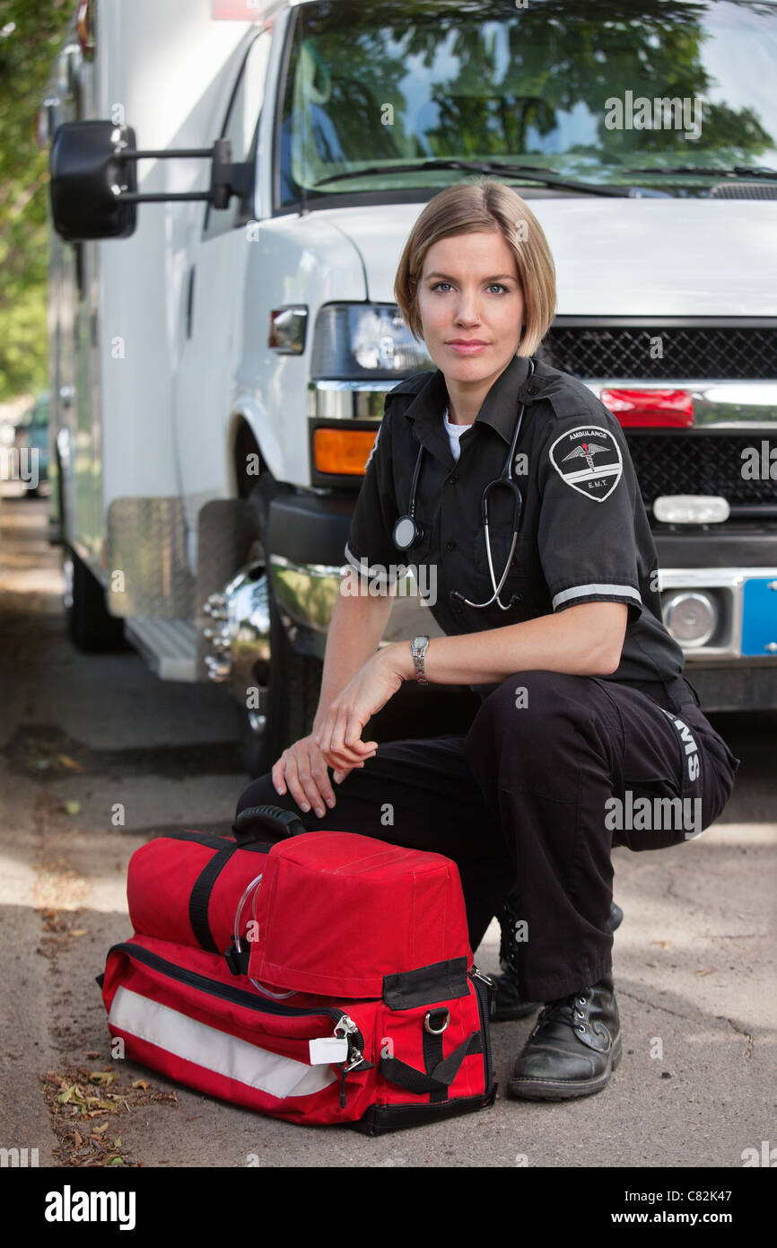 Confident EMS paramedic kneeling by portable oxygen unit and ambulance ...