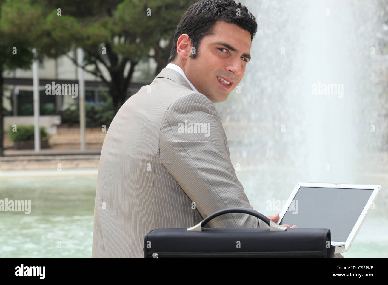 Businessman using a laptop computer outdoors by a fountain Stock Photo ...