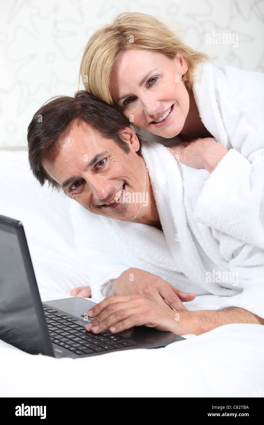 Happy couple on laptop in dressing gown Stock Photo - Alamy