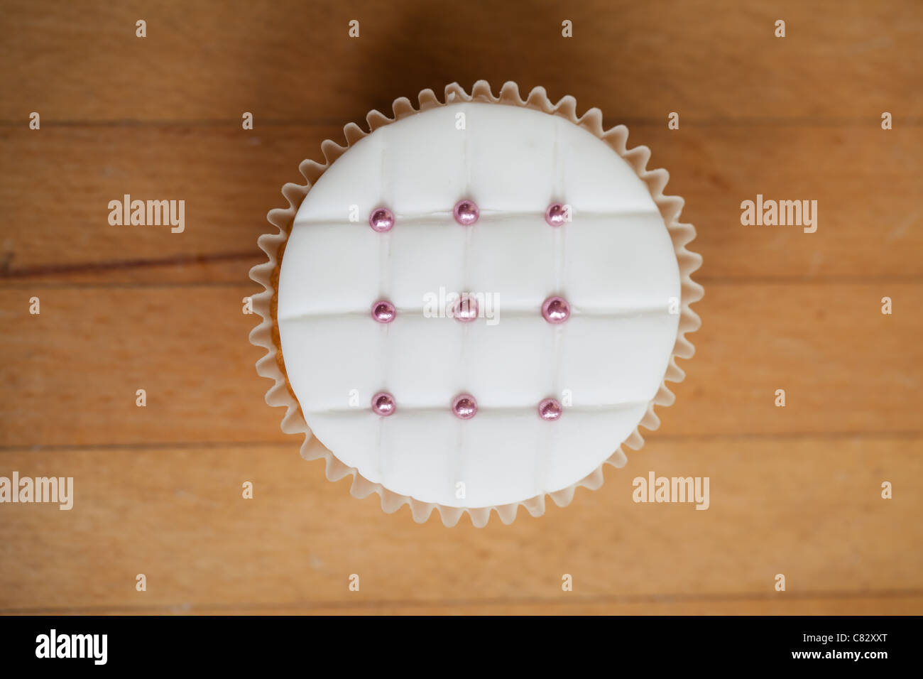 Top view of a cupcake on a wooden surface. Cake has white icing and 9 ...